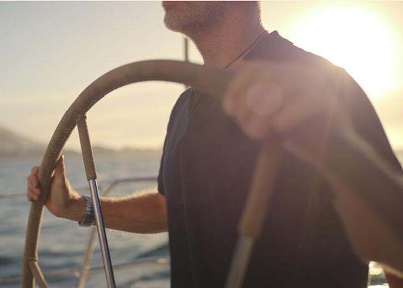 Sailor, man and steering boat with helm on vacation or summer holiday.